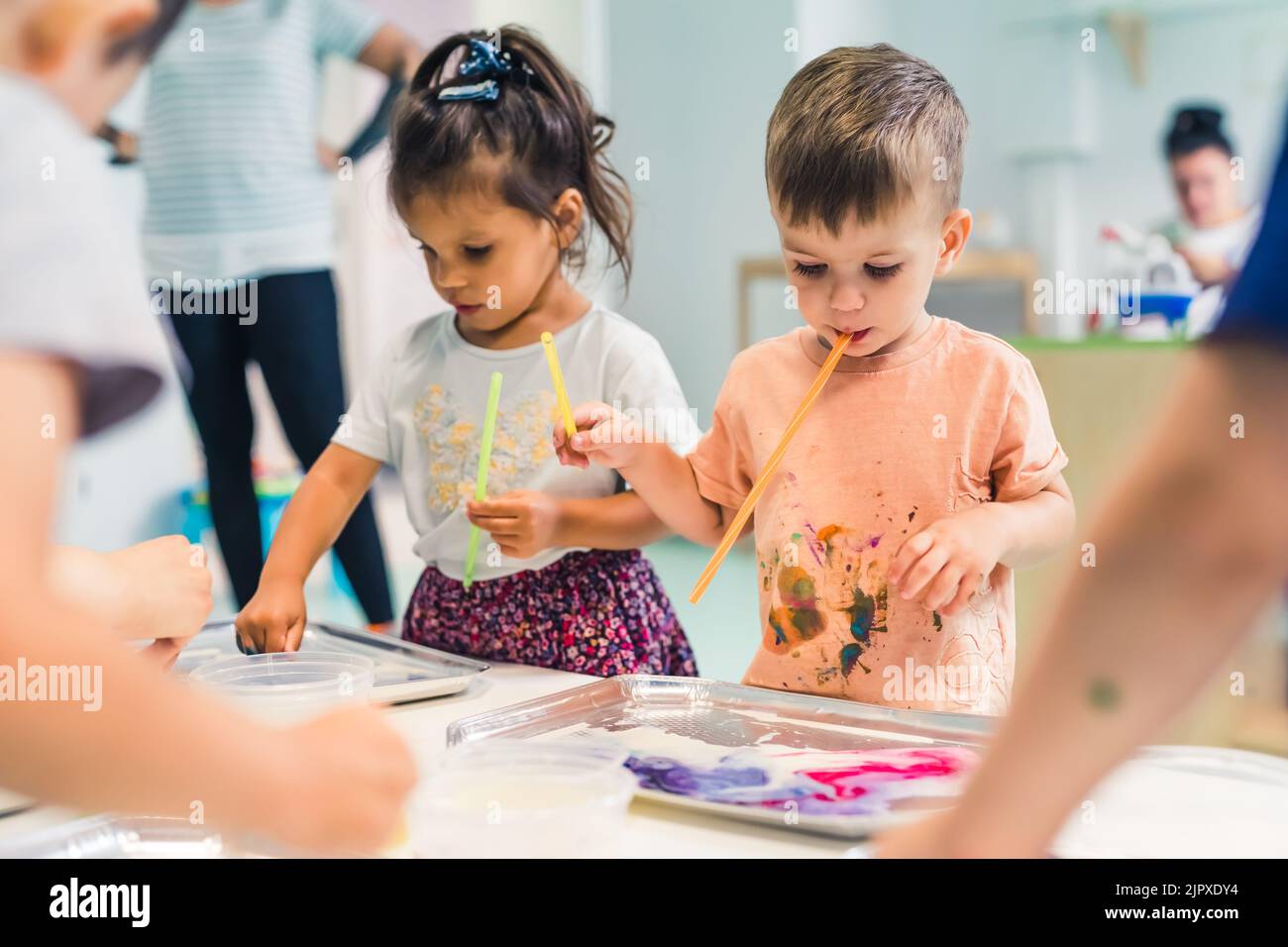 Multi-ethnic group of toddlers milk painting with the teacher helping ...
