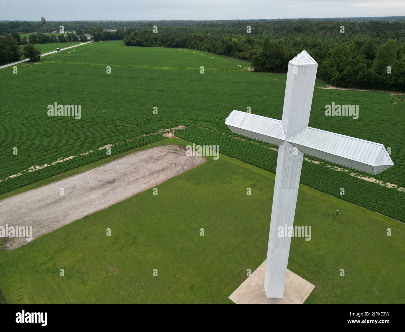 A huge, white cross in the middle of a field surrounded by forests ...