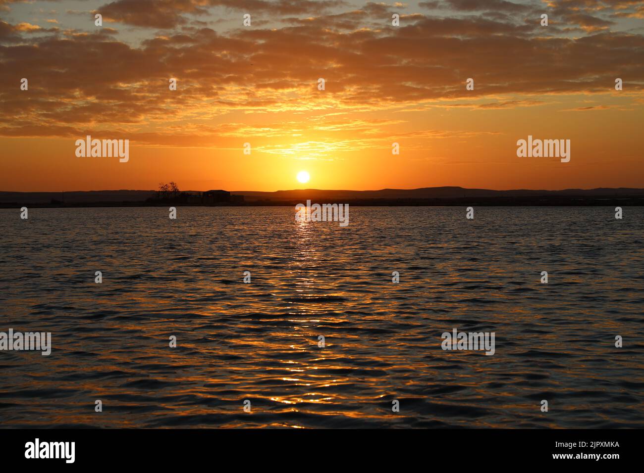 A scenic view of the shiny sea under the orange sunset sky Stock Photo ...