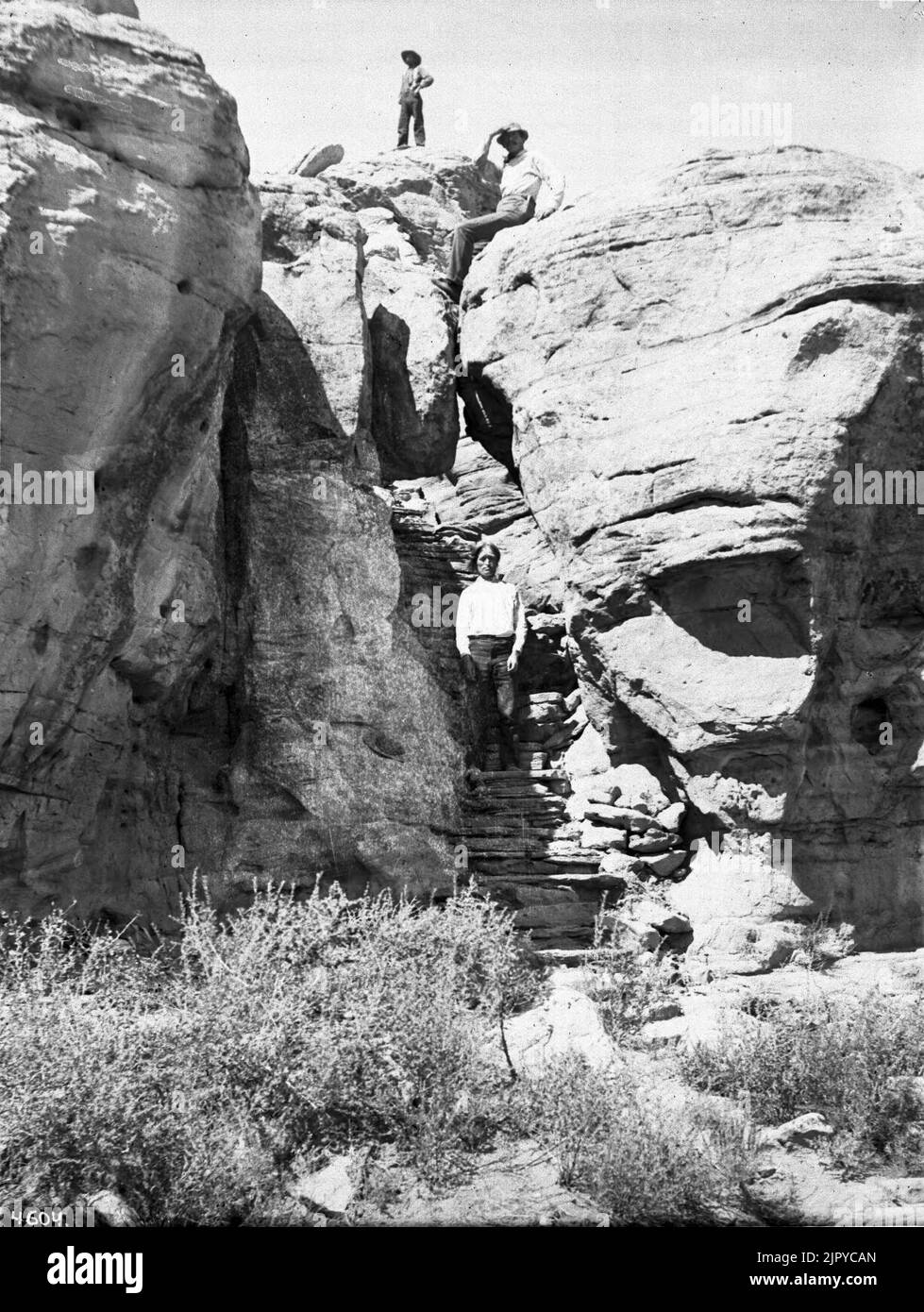 Three men climbing the foot trail to the top of the mesa of the Hopi ...