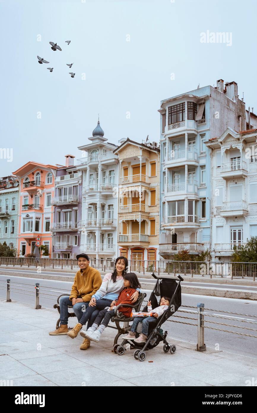 family sitting on a bench with beautiful building at the background ...