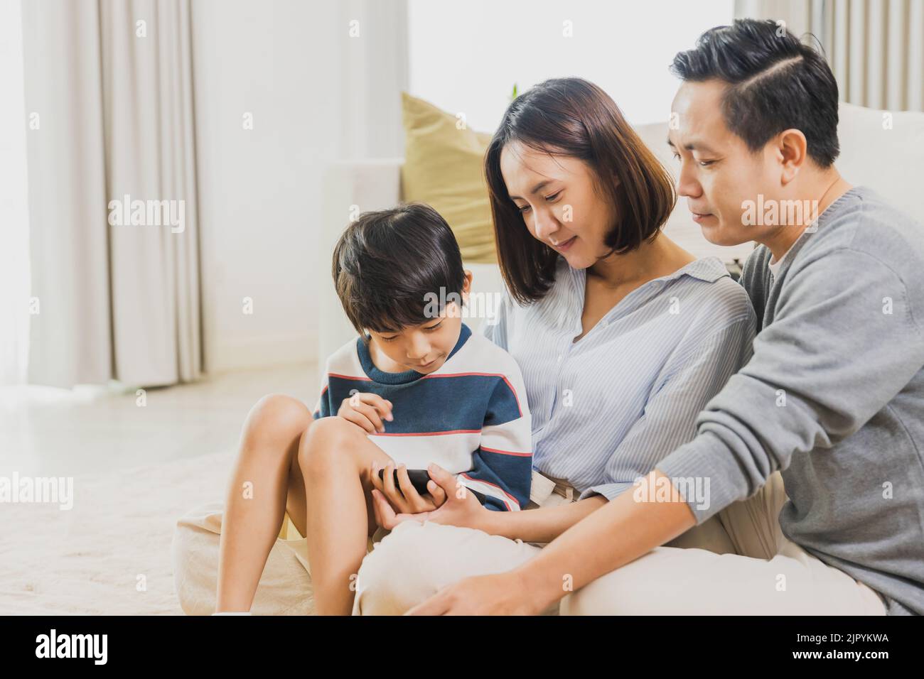 Close up happy Asian parents with son using phone sitting at home ...