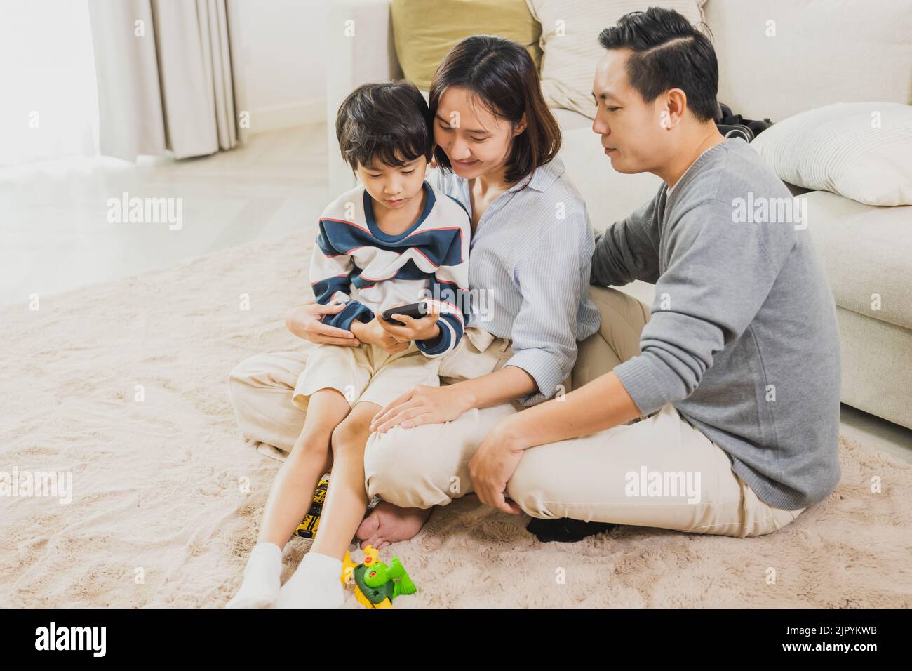 Happy Thai family in house, parents , mom, dad and boy watch on phone ...