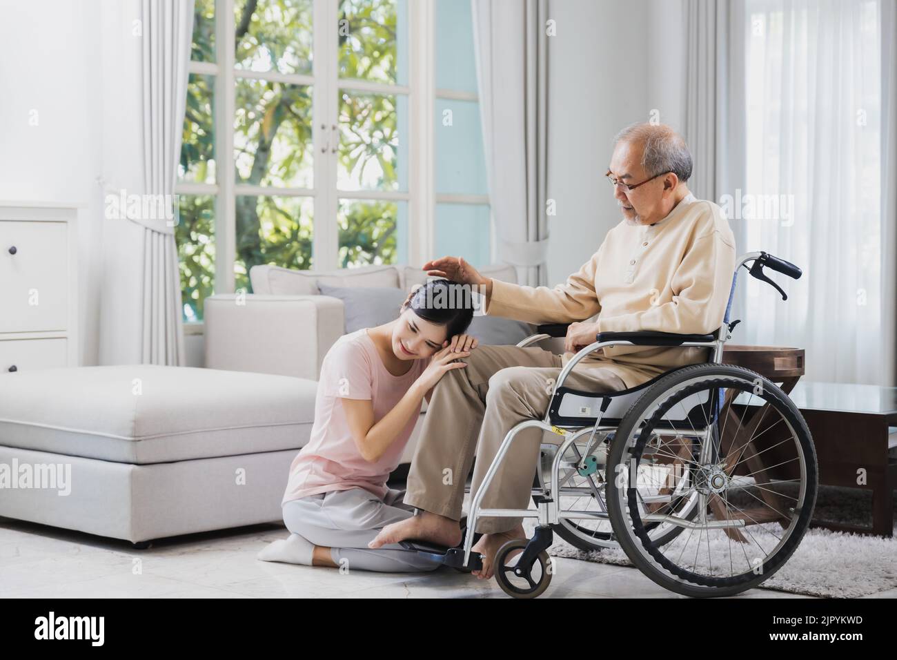 senior with beautiful daughter, old man sitting on wheelchair in house, caressing the head with ...