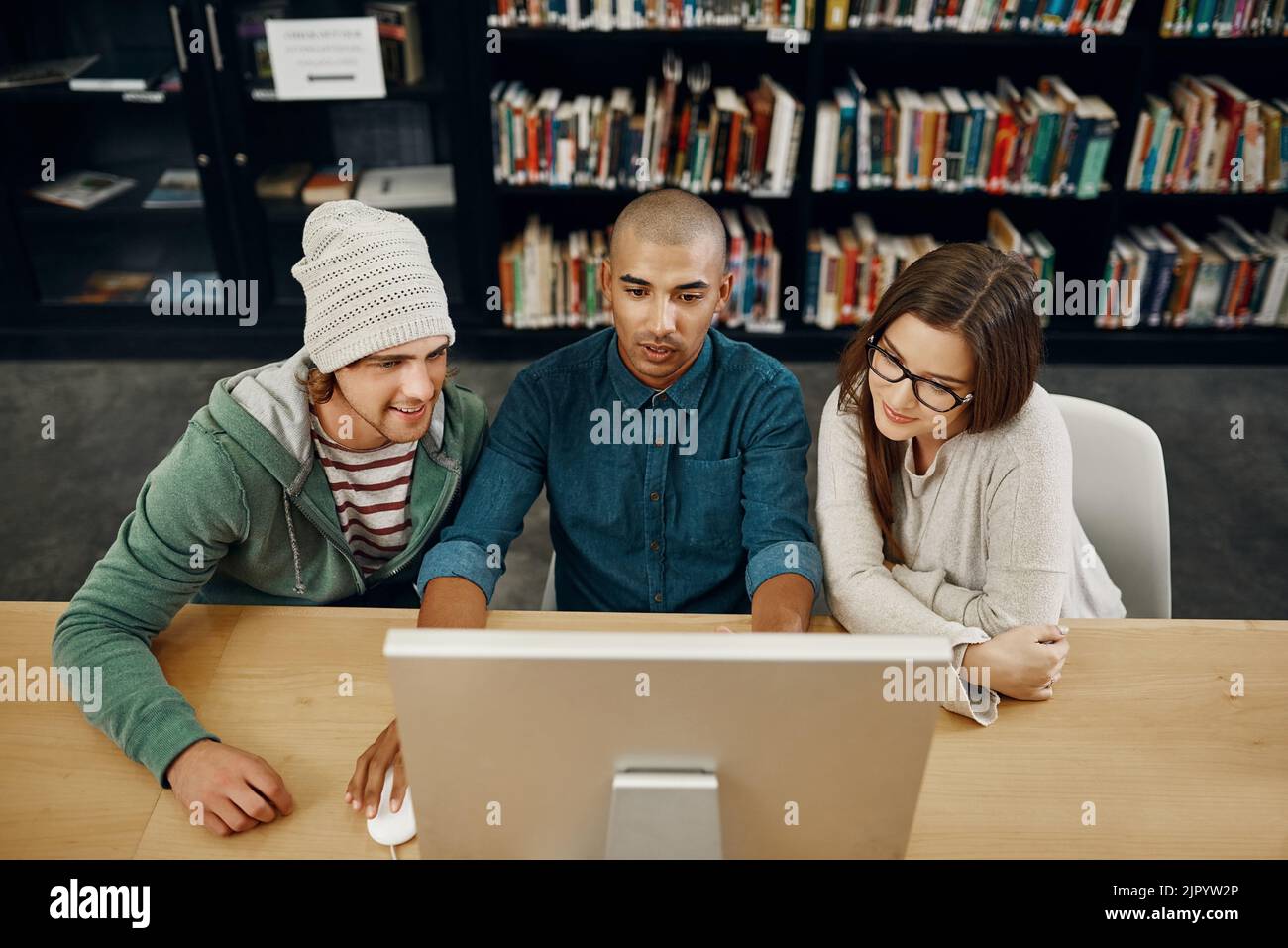 Studying together. High angle shot of three young university students studying in the library ...