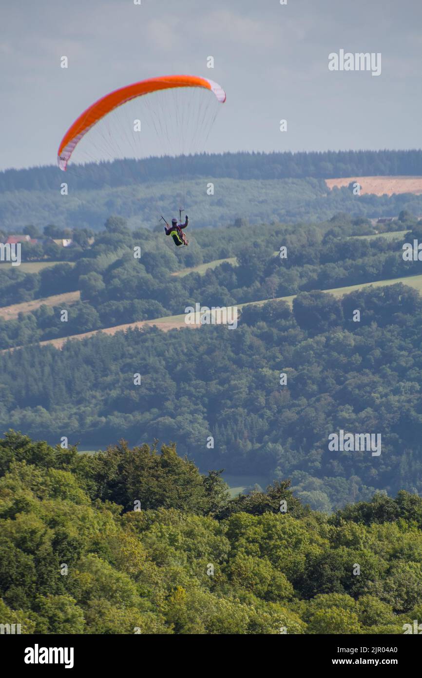 A vertical shot of a paraglider flying over mountains covered in trees ...