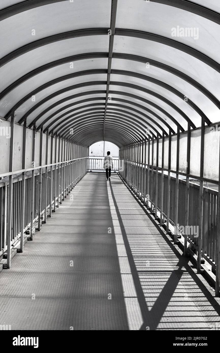 Black and white pedestrian bridge with one man at end, striped shadows ...
