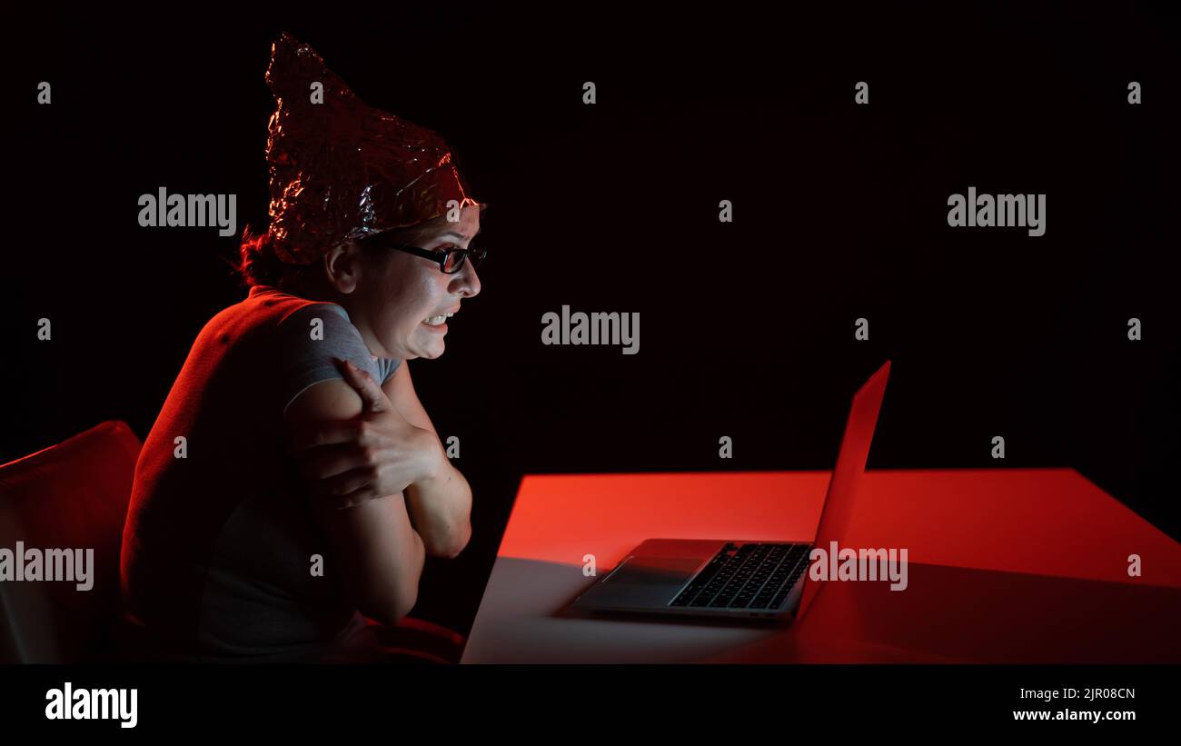 Paranoid caucasian woman typing on a computer wearing a tinfoil cap ...