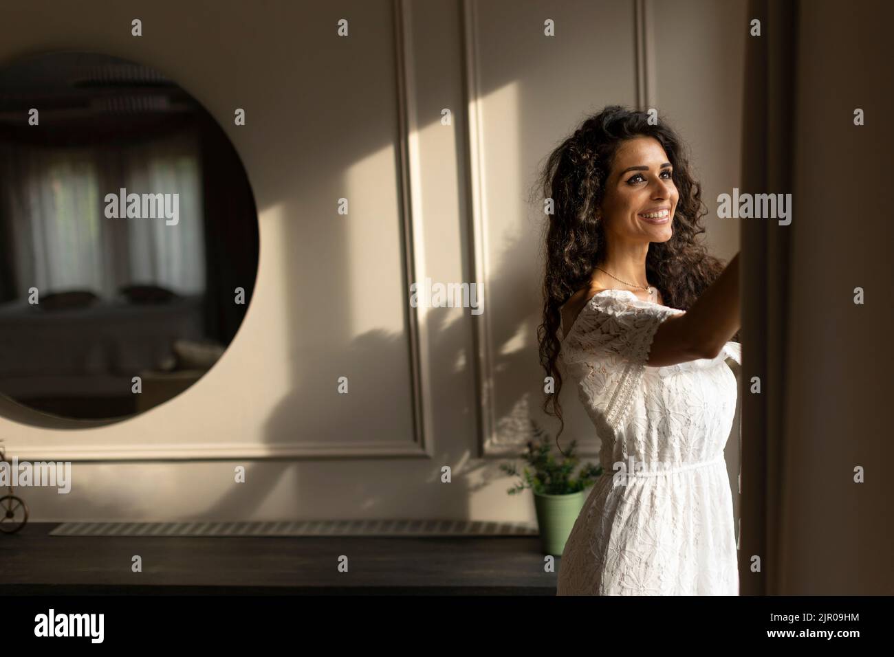 Pretty young curly hair woman standing by the window in the room Stock ...
