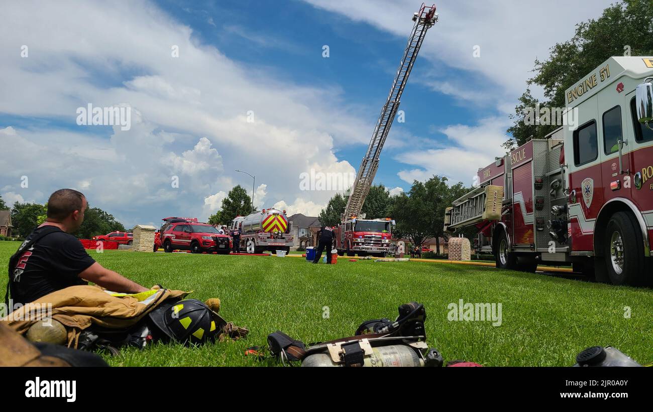 A firefighter sitting on the grass near red firefighting trucks and a ...