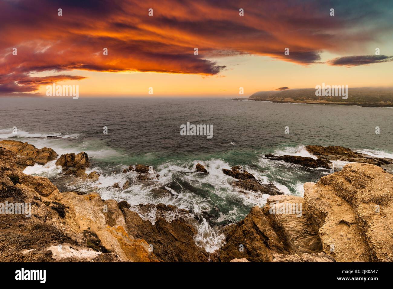 A rocky seashore with water washing over it under a sunset sky with ...