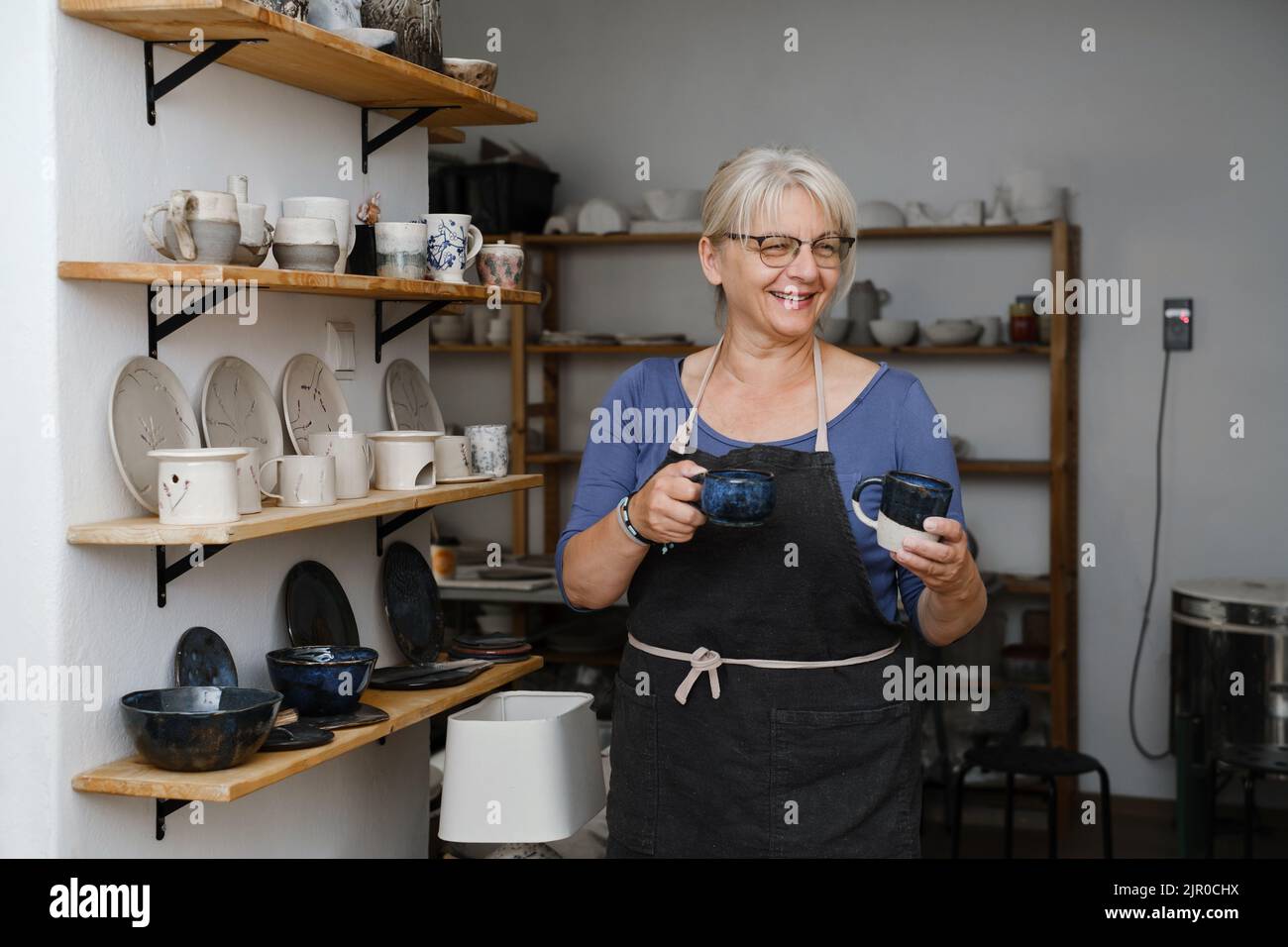 Potter artist showing her work in studio. Mature ceramist standing at ...