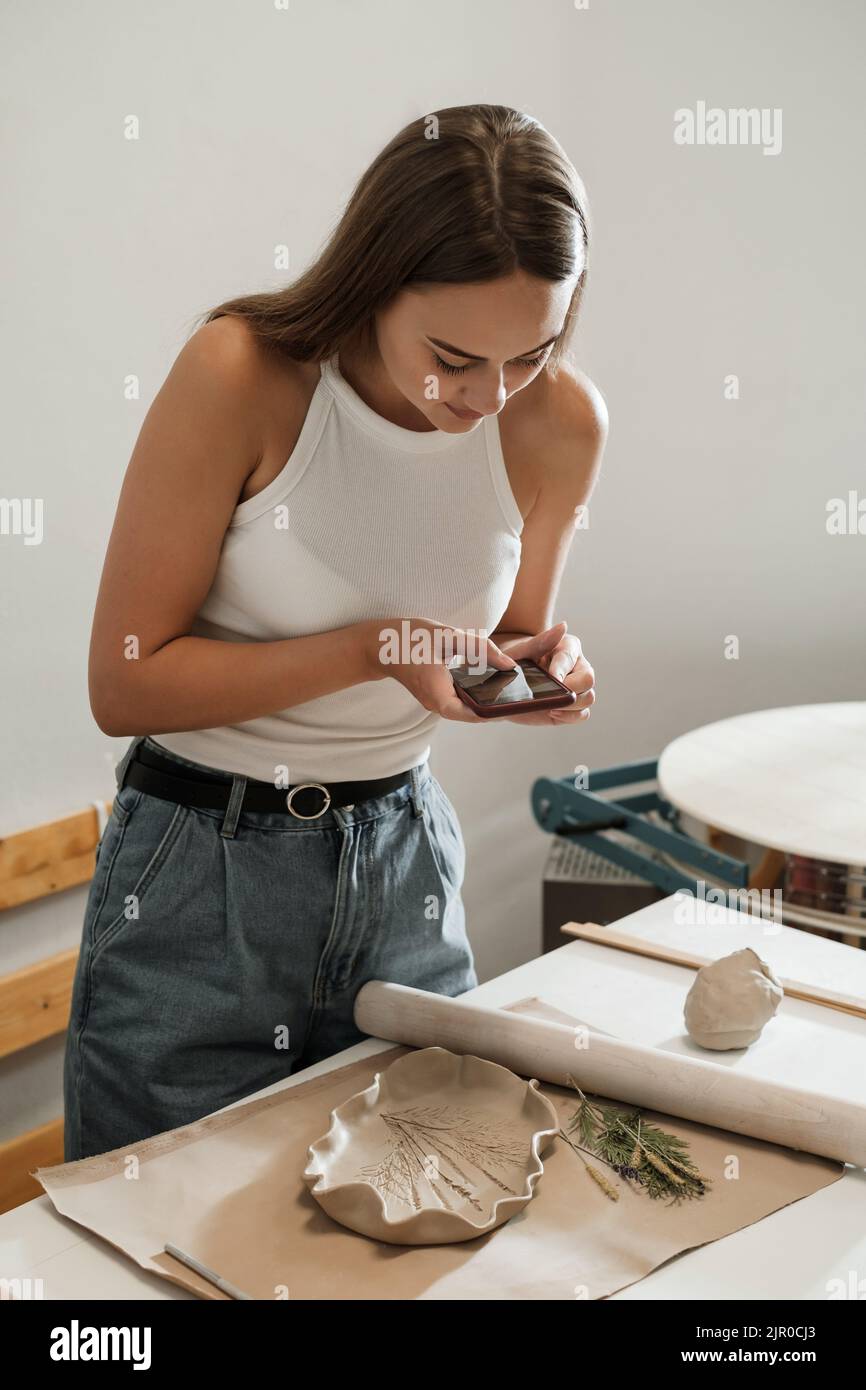 Taking picture of handmade ceramics on workshop. Pottery blog owner making photo of clay plate ...