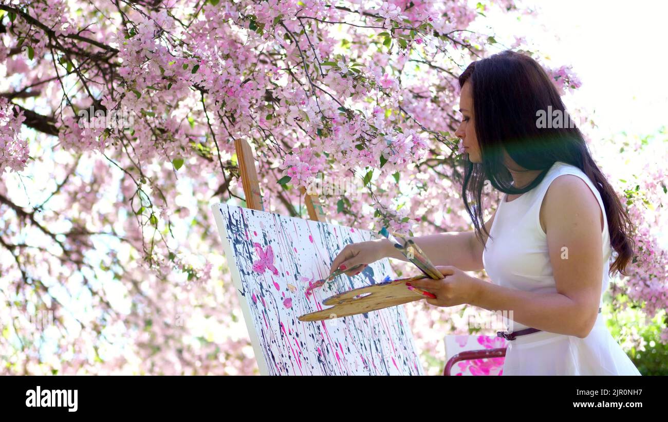 a beautiful woman painter in white dress, artist paints a picture of ...