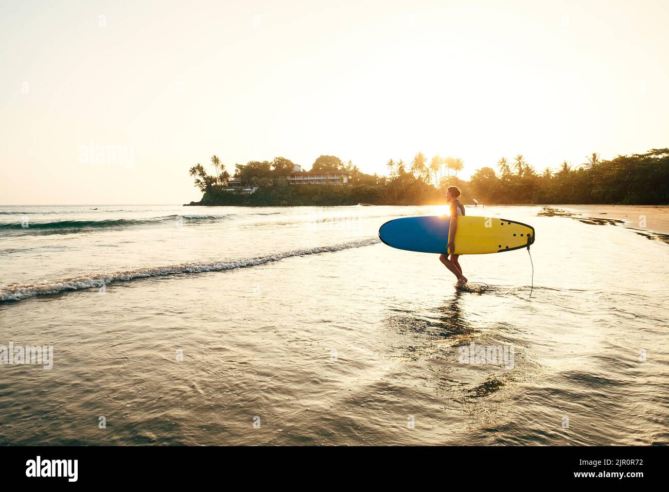 Teen boy with blue and yellow surfboard entering the waves for surfing ...