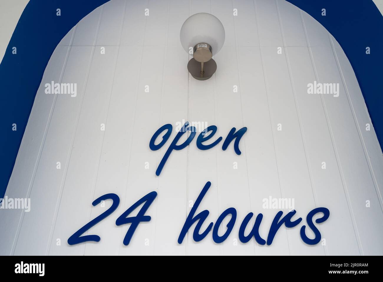 Blue color wording "Open 24 hours" showing on the white wall. A lamp is ...