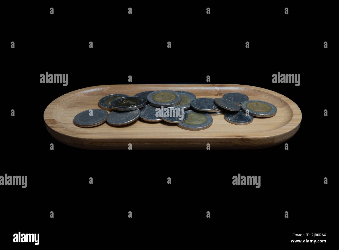 Coins of different value on a wooden plate on a black background ...