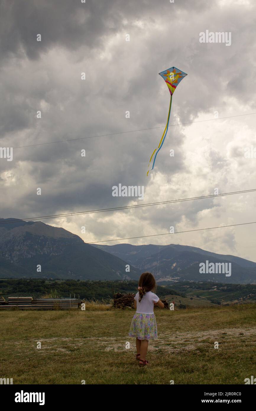 Adorable little girl playing in an open field with a kite with a cloudy ...