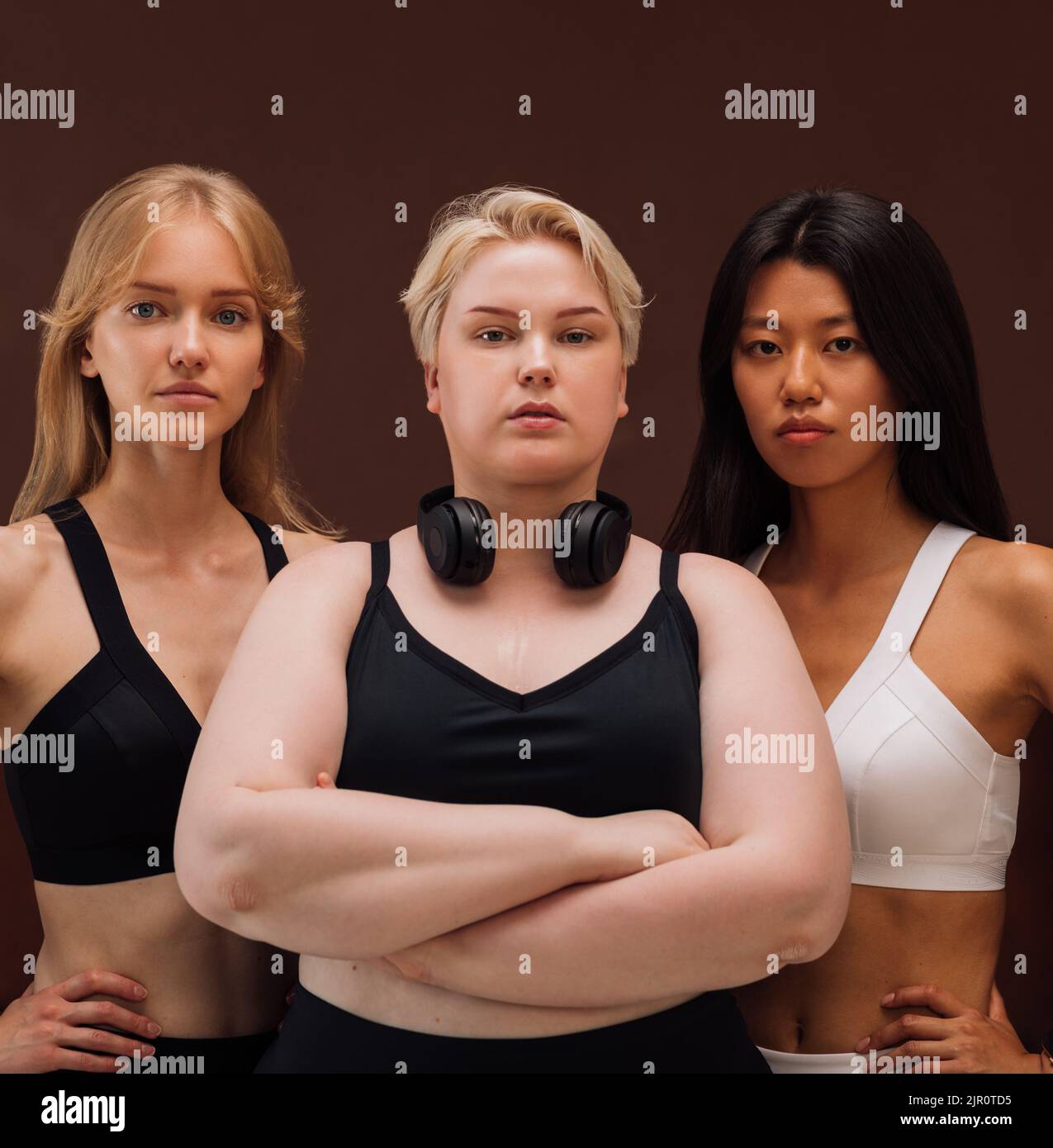 Three women with different body types standing together against brown ...