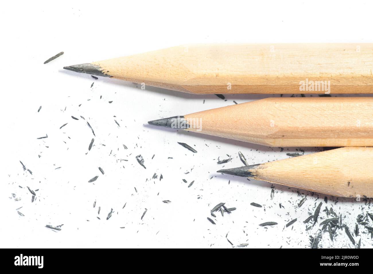 Three sharpened pencils with graphite shavings on white background ...