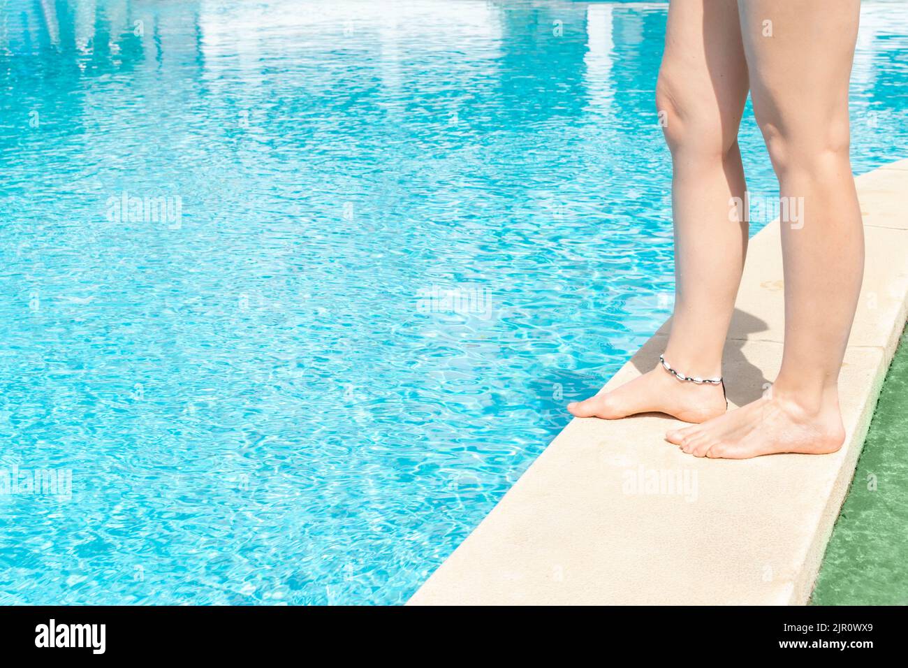 A closeup of a barefoot woman's legs standing at the edge of a swimming ...
