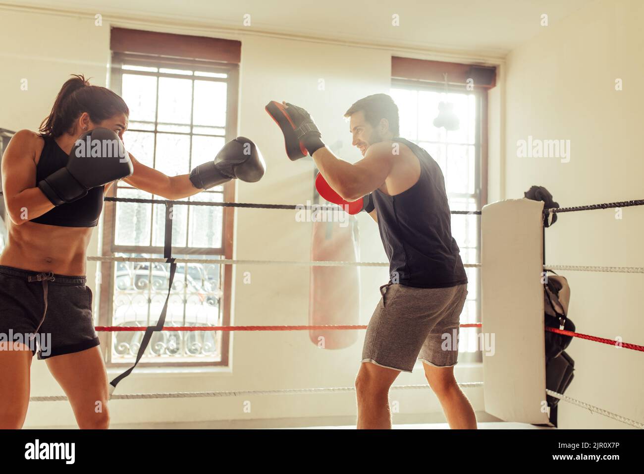 Muscular female boxer striking focus mitts held by her personal trainer ...