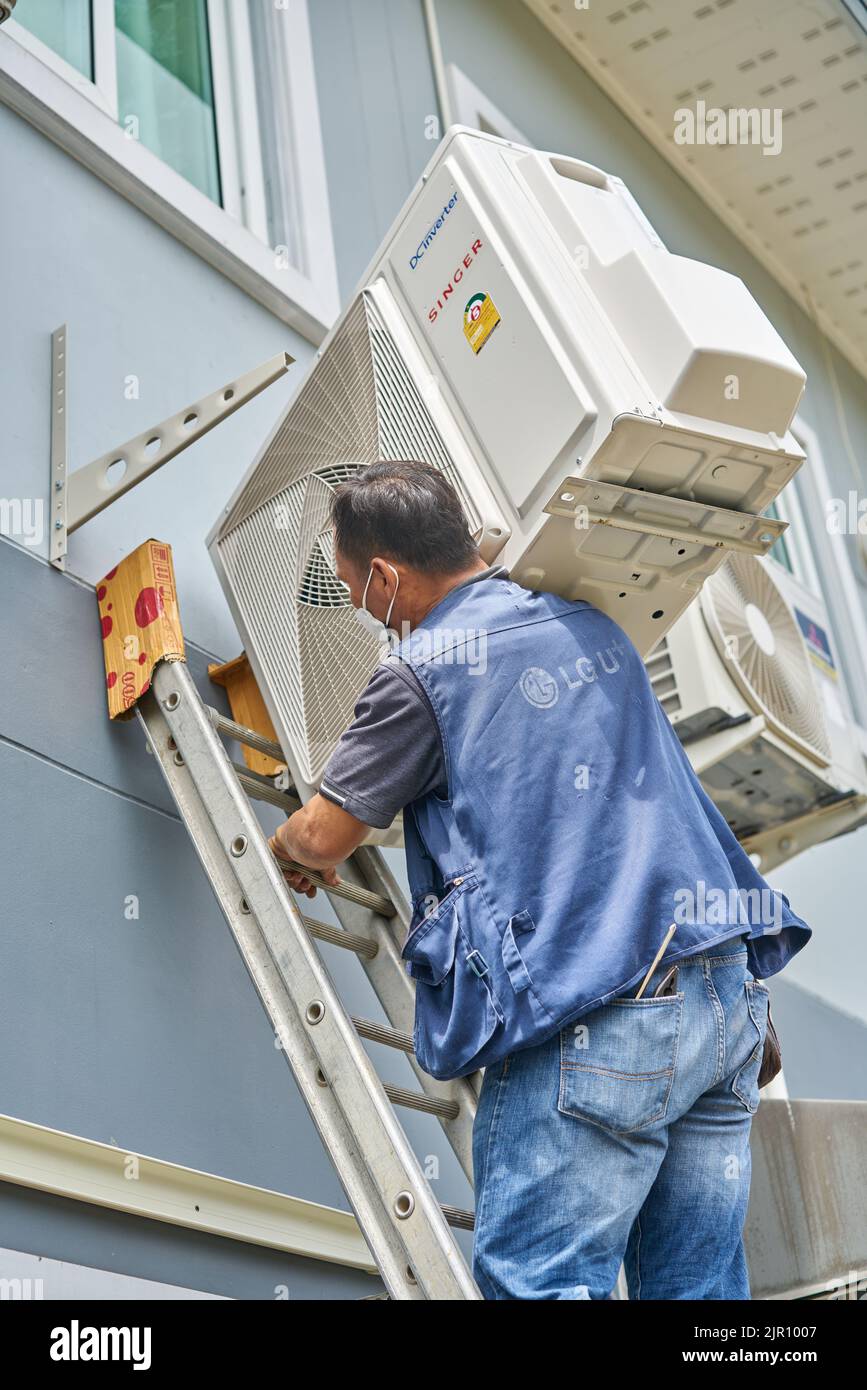 A man carries a heavy air conditioner compressor on his shoulder while ...