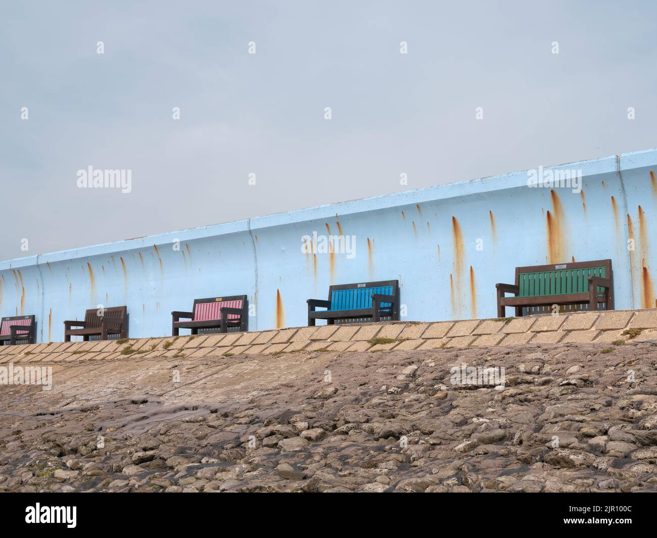 The empty coloured public benches and painted seawall flood defence at ...