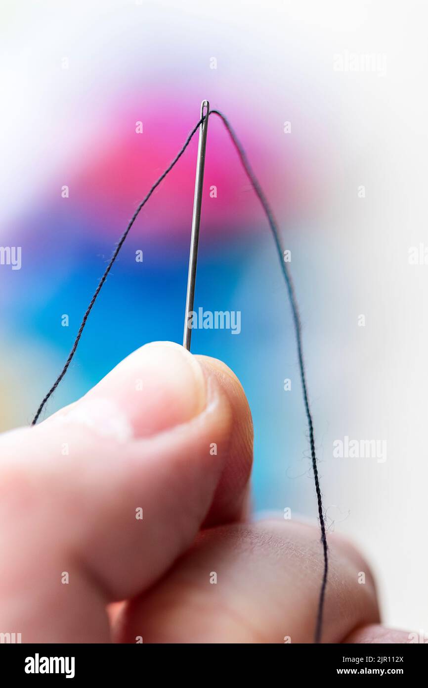 A portait of two fingers holding a metal sewing needle with a thread ...
