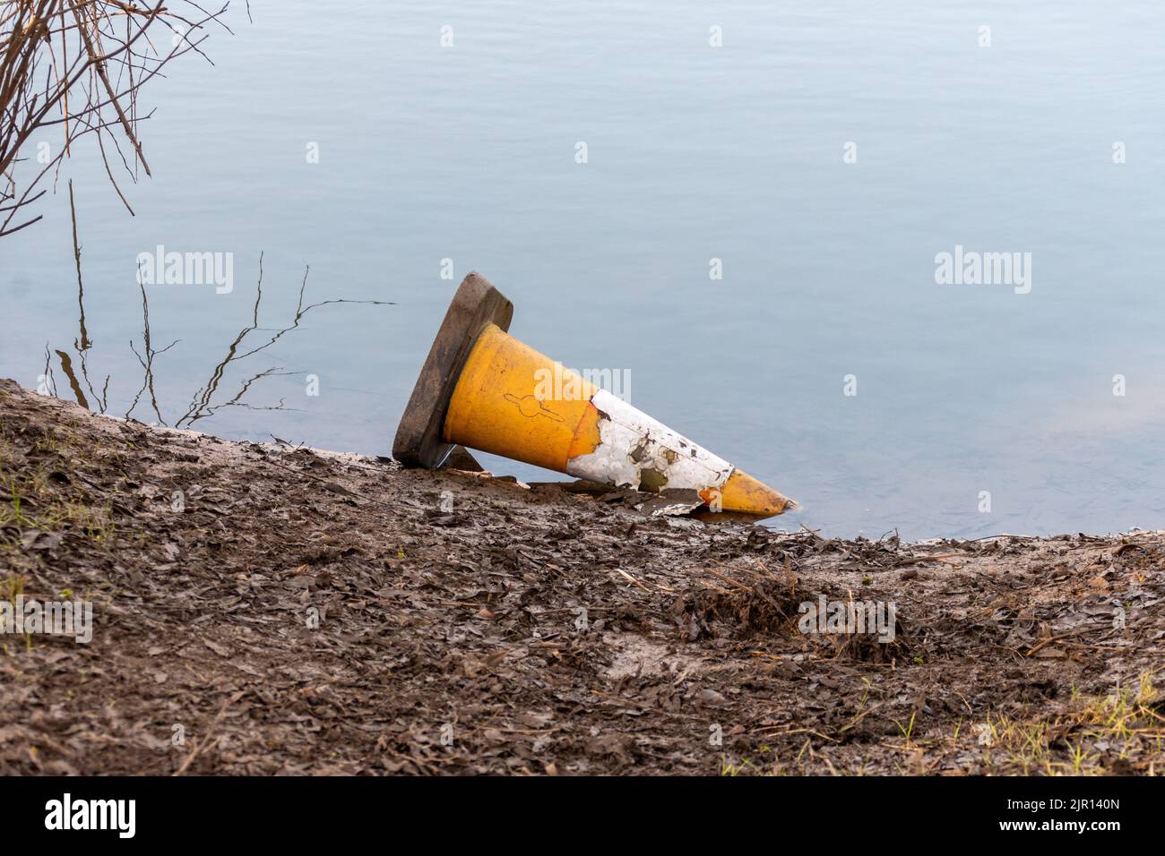 A tatty discarded traffic cone lying on its side in some shallow water ...