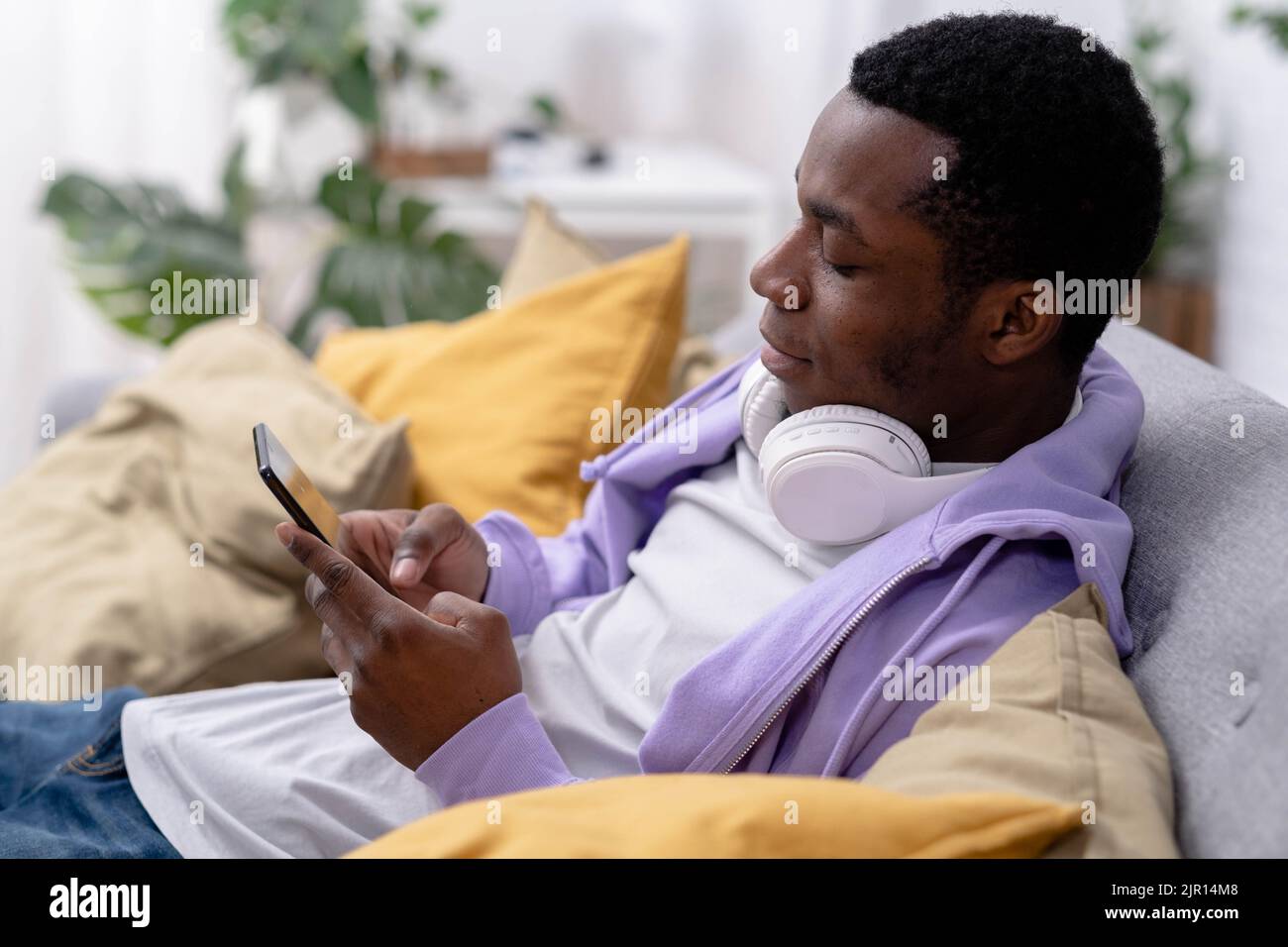 Black young man using smartphone at home sitting on couch, pressing ...