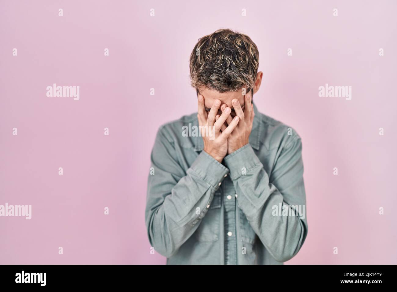 Hispanic man with beard standing over pink background with sad ...