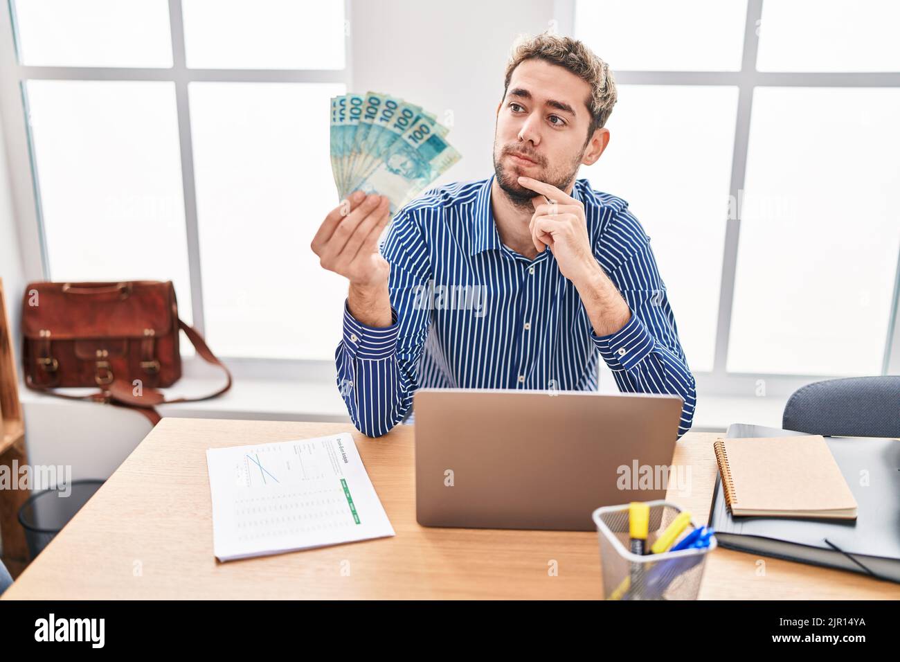 Hispanic man with beard working at the office holding brazilian reals ...