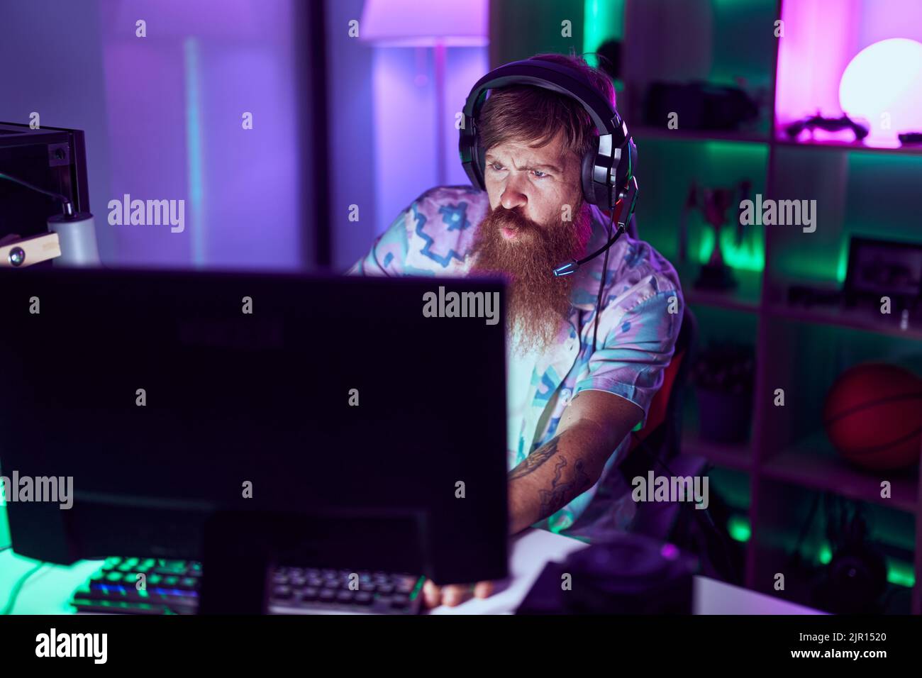 Young redhead man streamer playing video game using computer at gaming ...