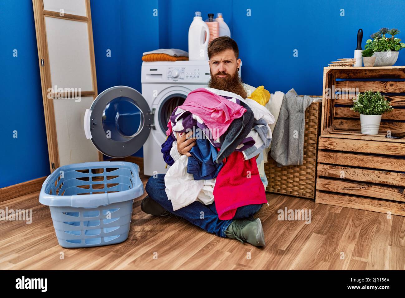 Redhead man with long beard putting dirty laundry into washing machine ...