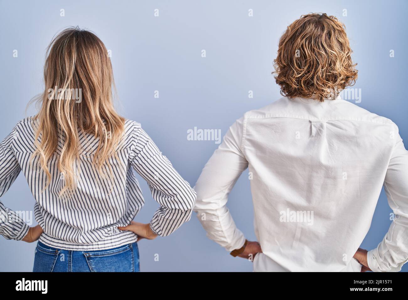 Young couple standing over blue background standing backwards looking ...