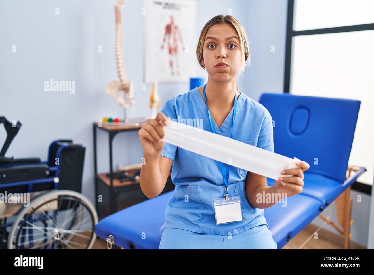 Young blonde woman holding therapy strip band puffing cheeks with funny ...