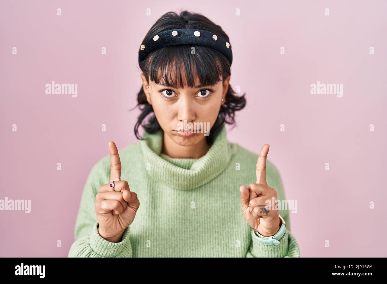 Young beautiful woman standing over pink background pointing up looking ...