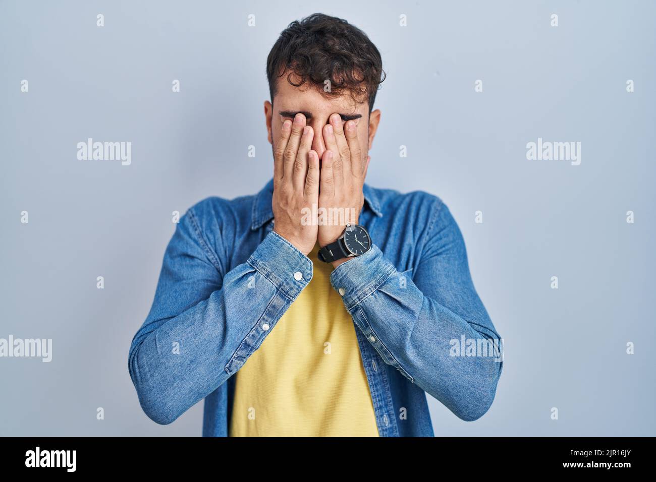 Young hispanic man standing over blue background rubbing eyes for ...