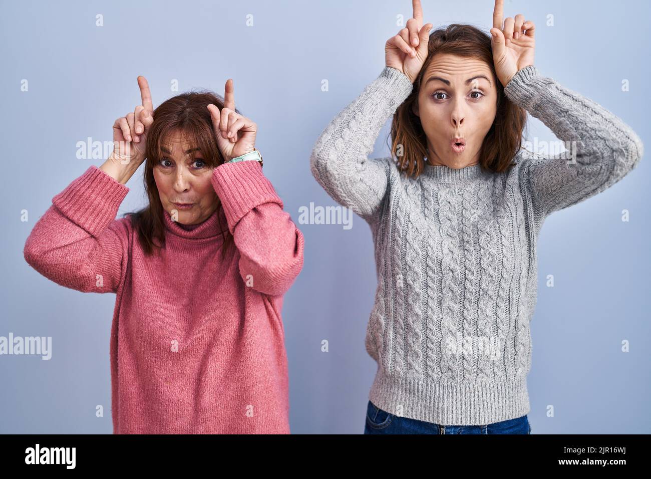 Mother And Daughter Standing Over Blue Background Doing Funny Gesture