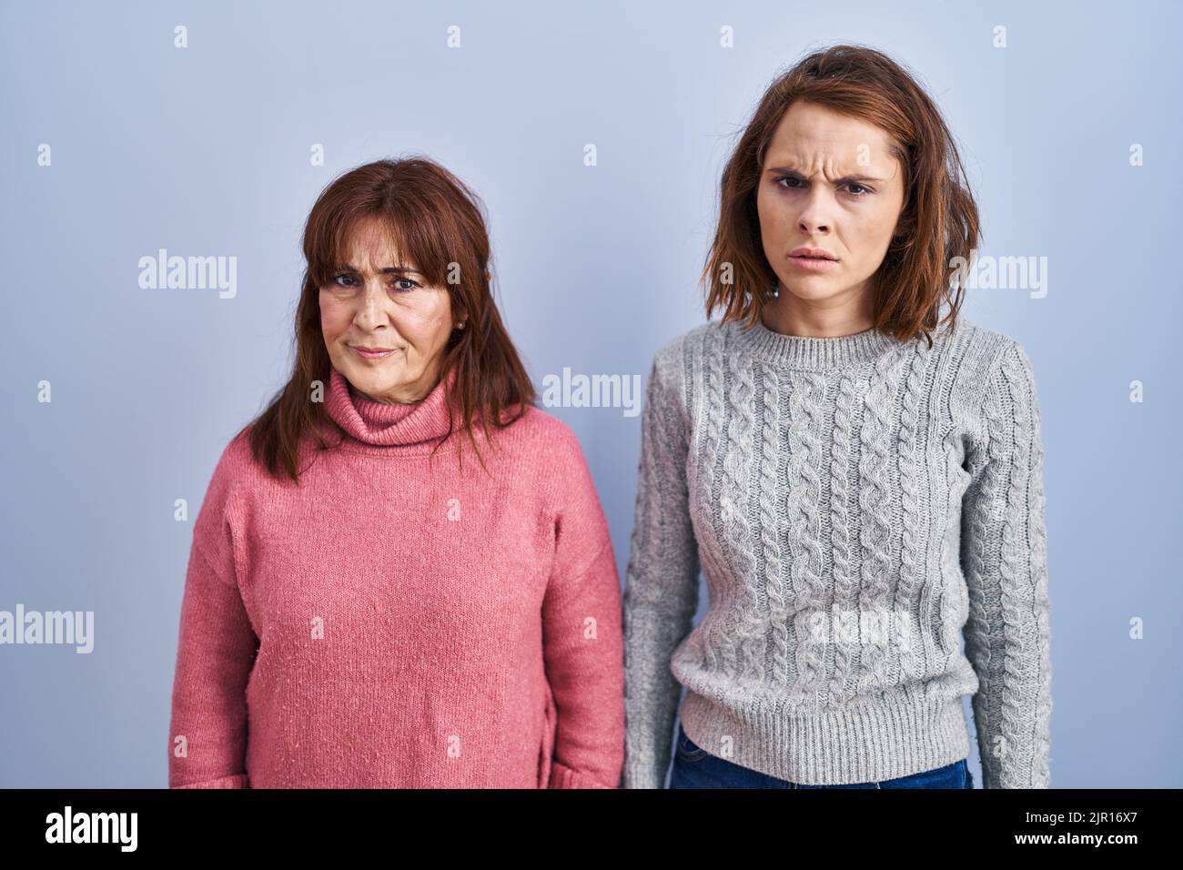 Mother And Daughter Standing Over Blue Background Skeptic And Nervous
