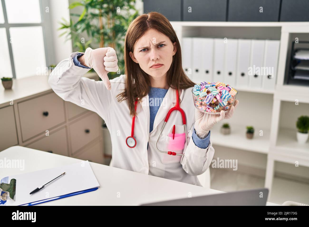Young doctor woman holding sweets candy with angry face, negative sign ...