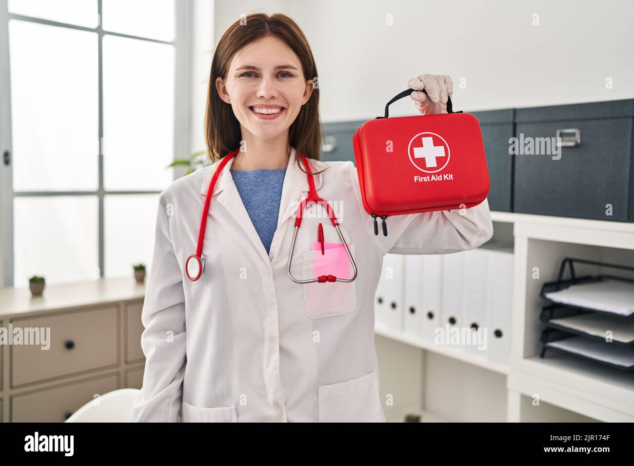 Young doctor woman holding first aid kit looking positive and happy ...