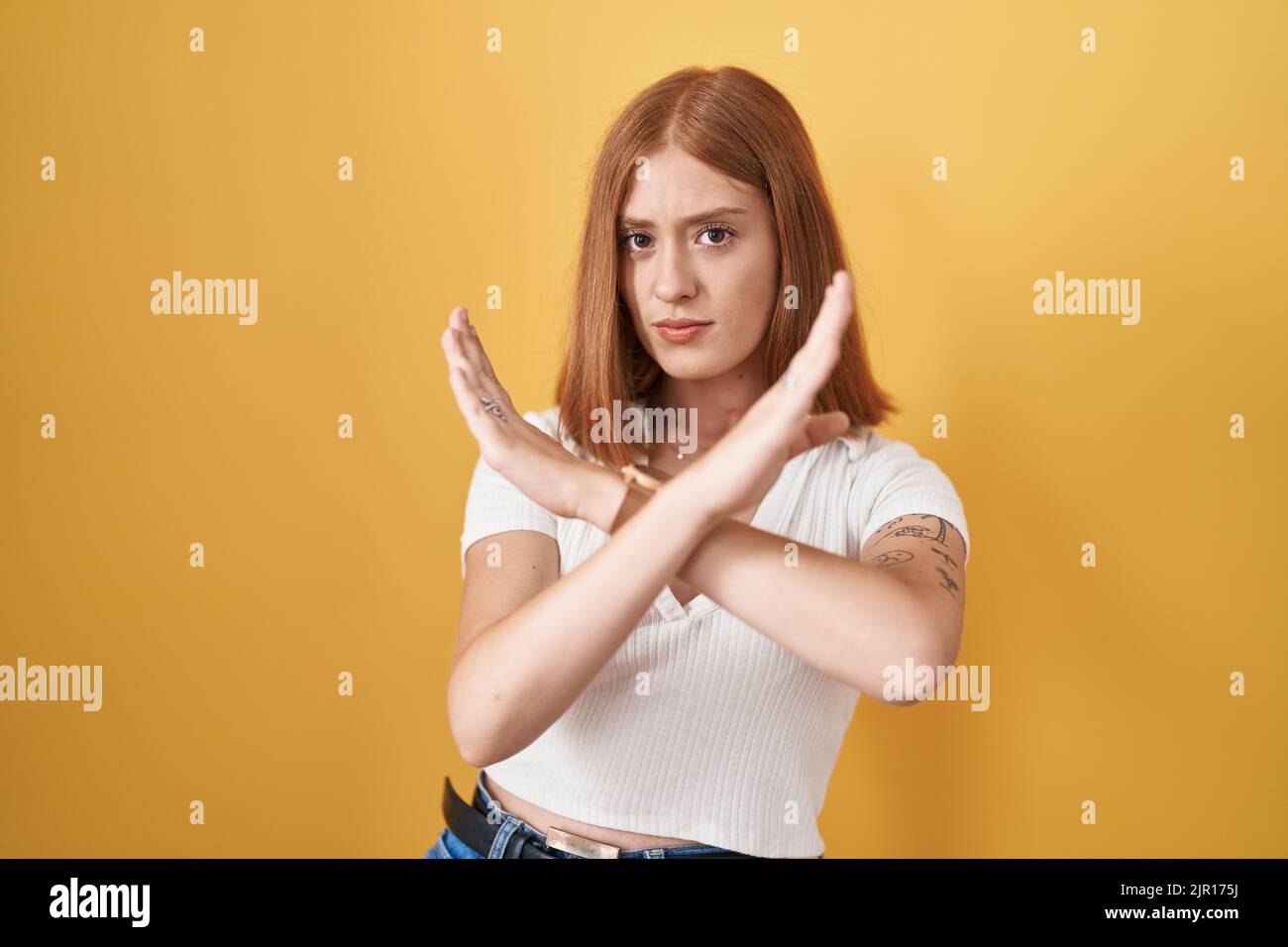 Young redhead woman standing over yellow background rejection ...