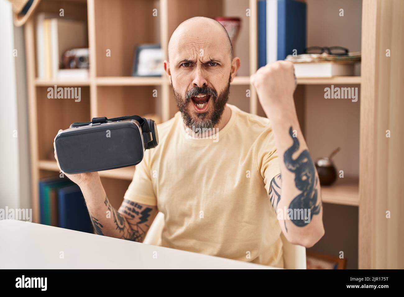 Young hispanic man wearing virtual reality glasses annoyed and frustrated shouting with anger ...