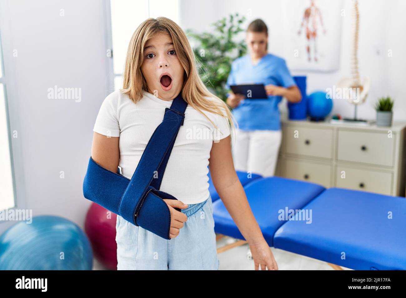 Blonde little girl wearing arm on sling at rehabilitation clinic scared ...