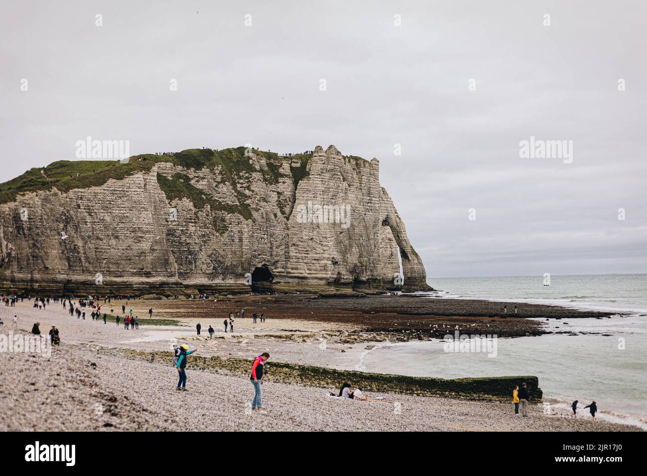 A group of tourists in warm clothes on the beach near a rocky cliff ...