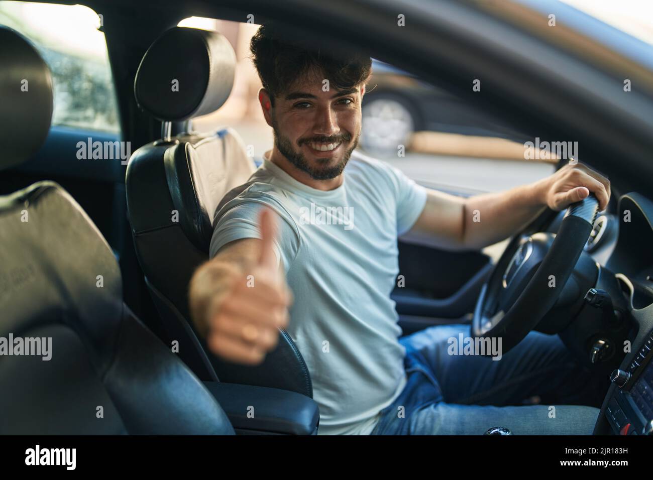 Young hispanic man driving car doing ok gesture with thumb up at street ...