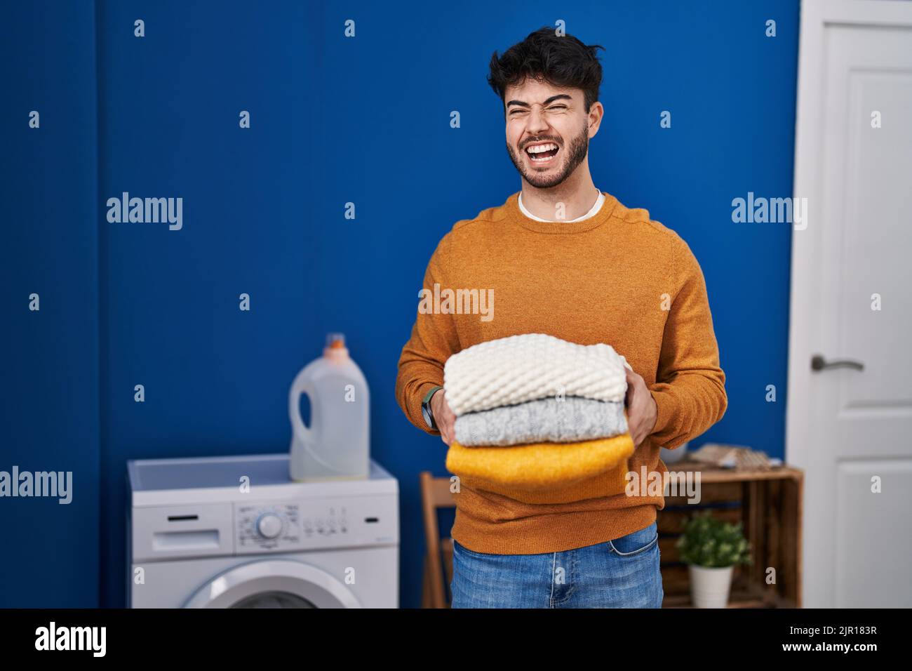 Hispanic man with beard holding clean folded laundry angry and mad ...