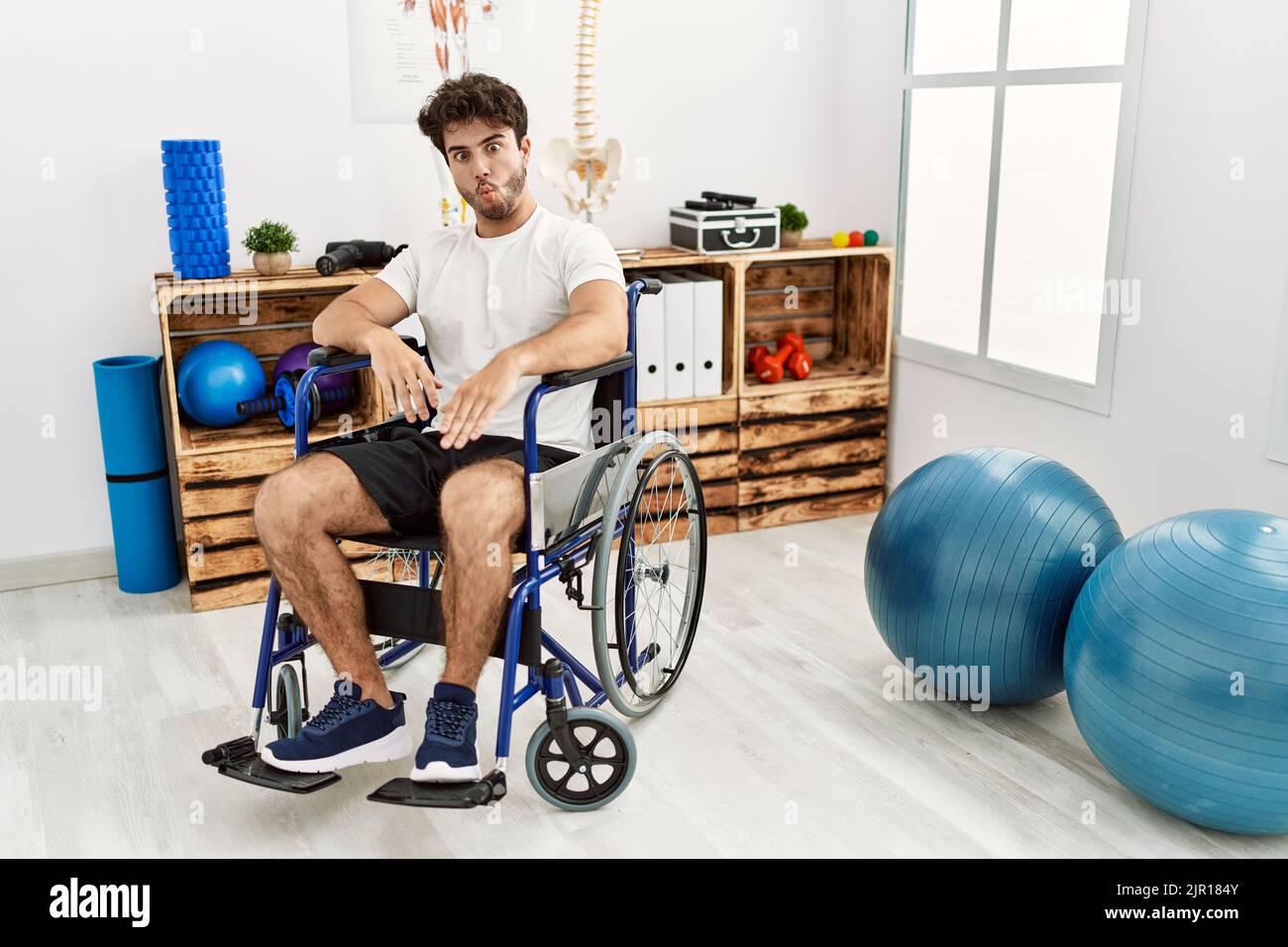 Hispanic man sitting on wheelchair at physiotherapy clinic making fish ...